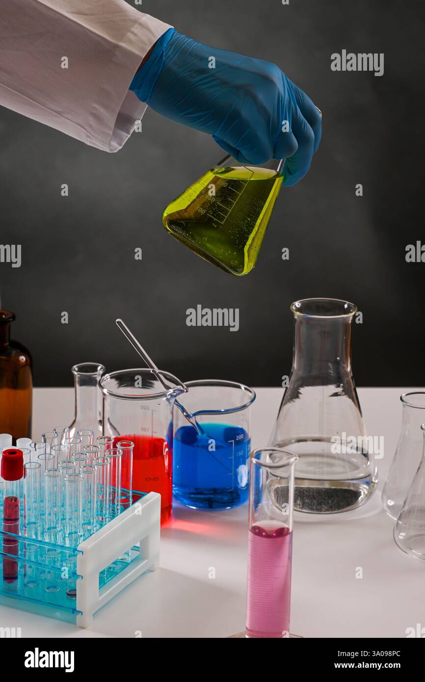 Gloved hand pouring yellow chemical liquid in erlenmeyer flask during a ...