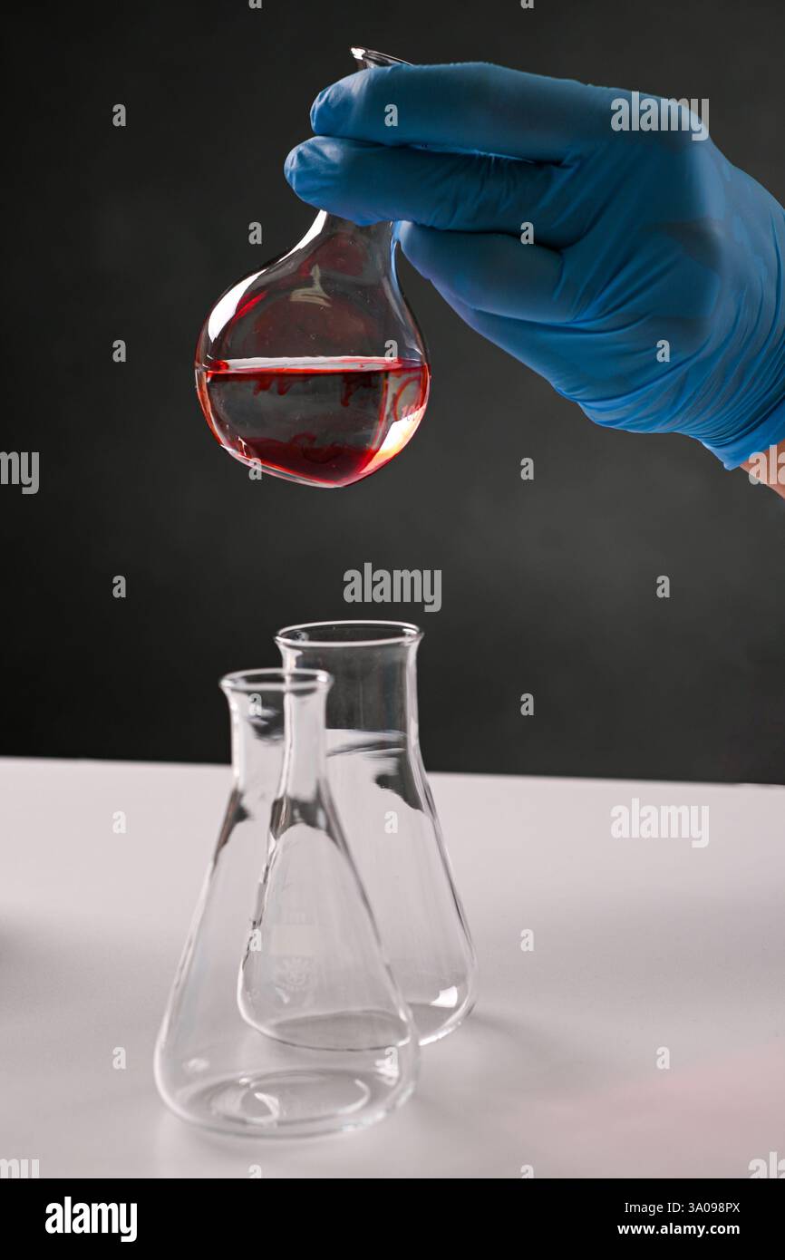 Gloved hand pouring red liquid from laboratory glassware into other ...