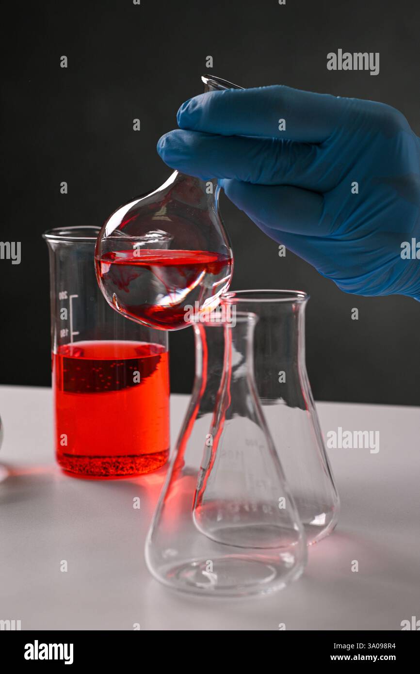 Gloved hand pouring red liquid from laboratory glassware into other ...
