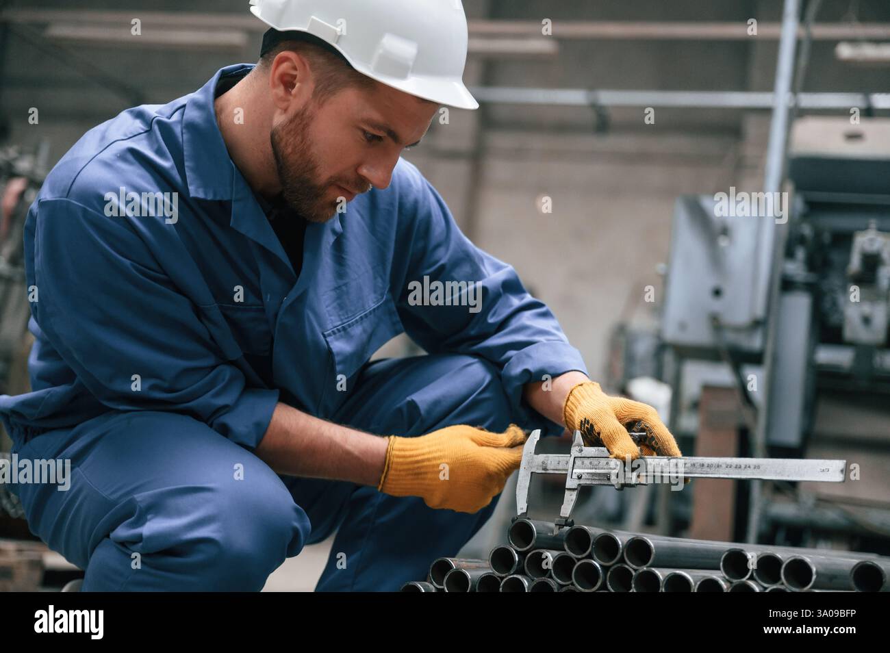 Using calliper to measure metal pipe. Factory worker in blue uniform is ...