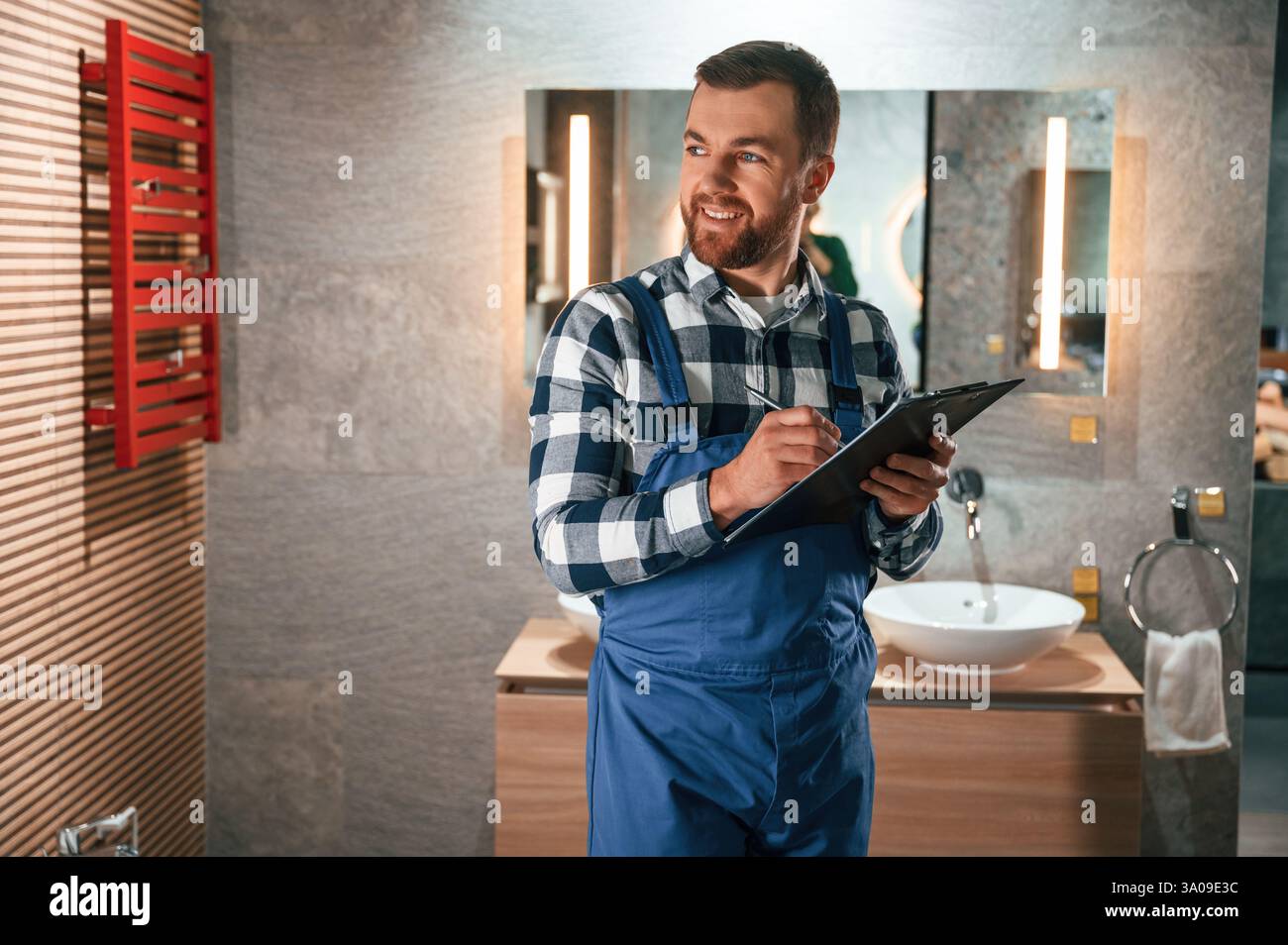With notepad in hands. Plumber in blue uniform is at work in the ...