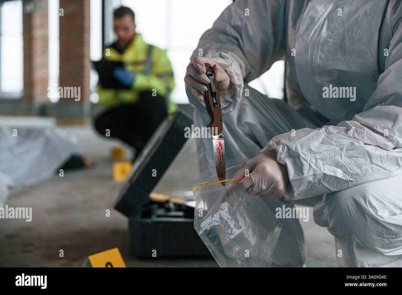 Putting the knife into bag. Detectives are collecting evidence in a crime scene near dead body ...