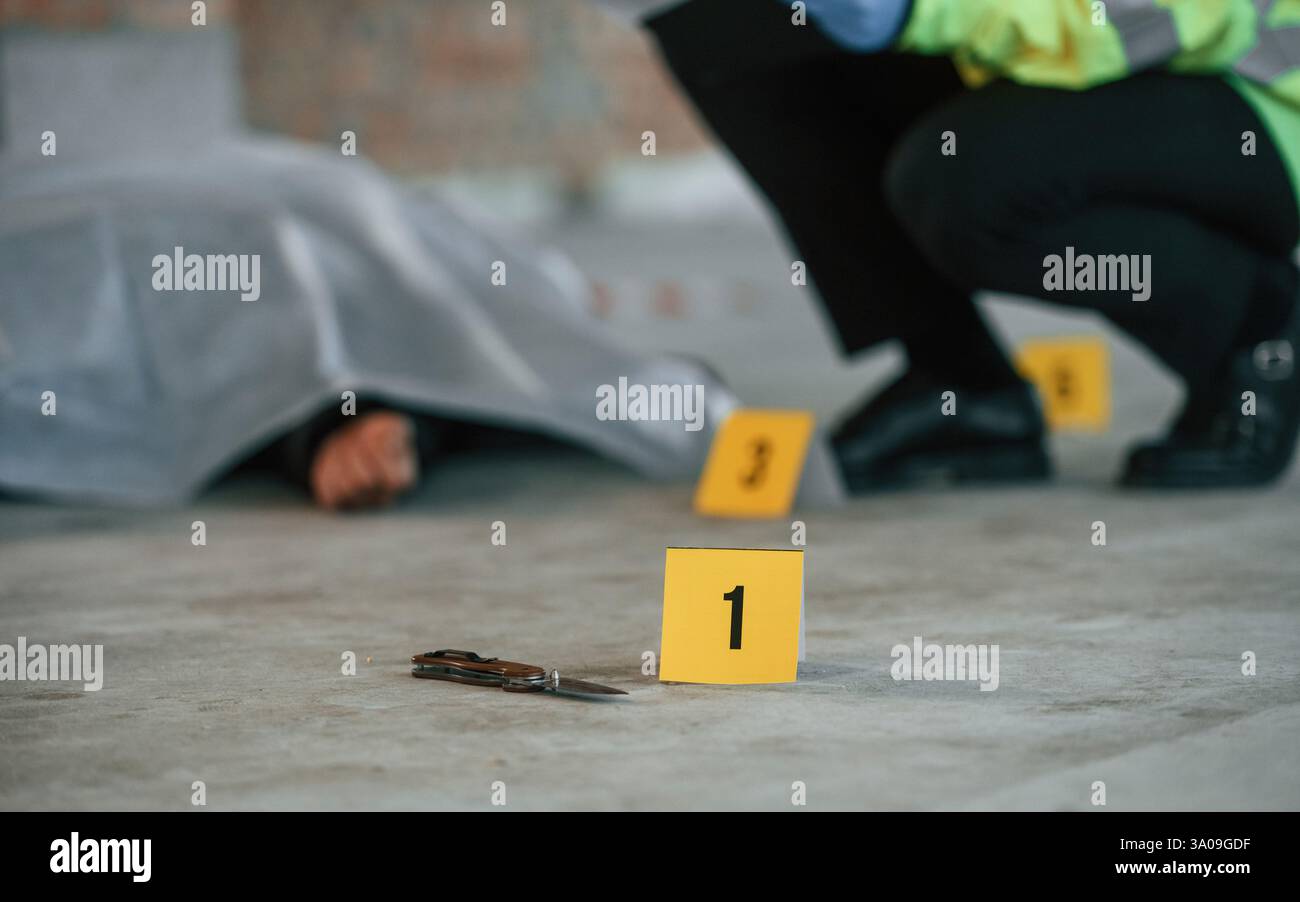 Male detective is collecting evidence in a crime scene near dead body on the construction site ...