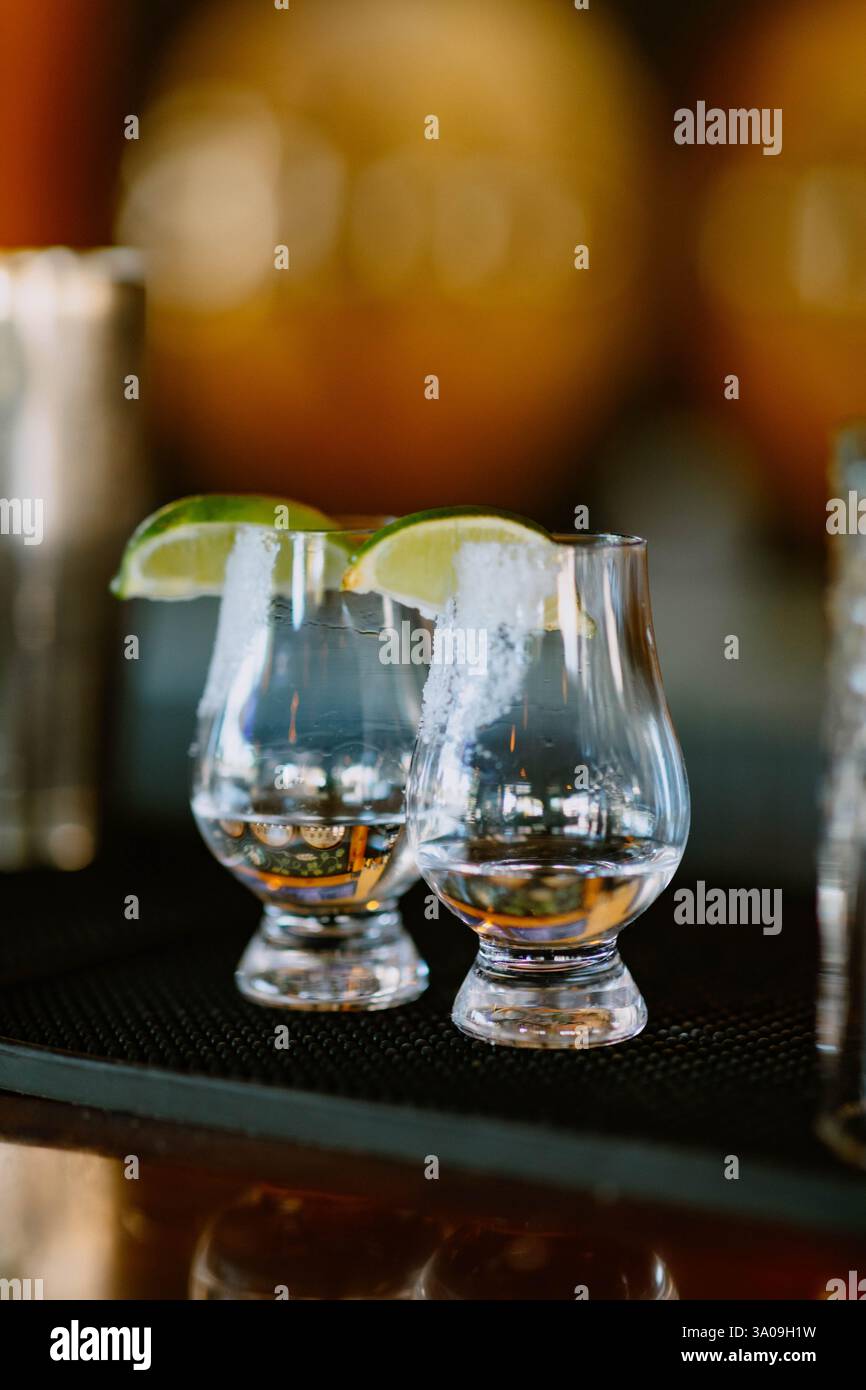 Two tequila shots with salted rims and lime wedges on a bar counter ...