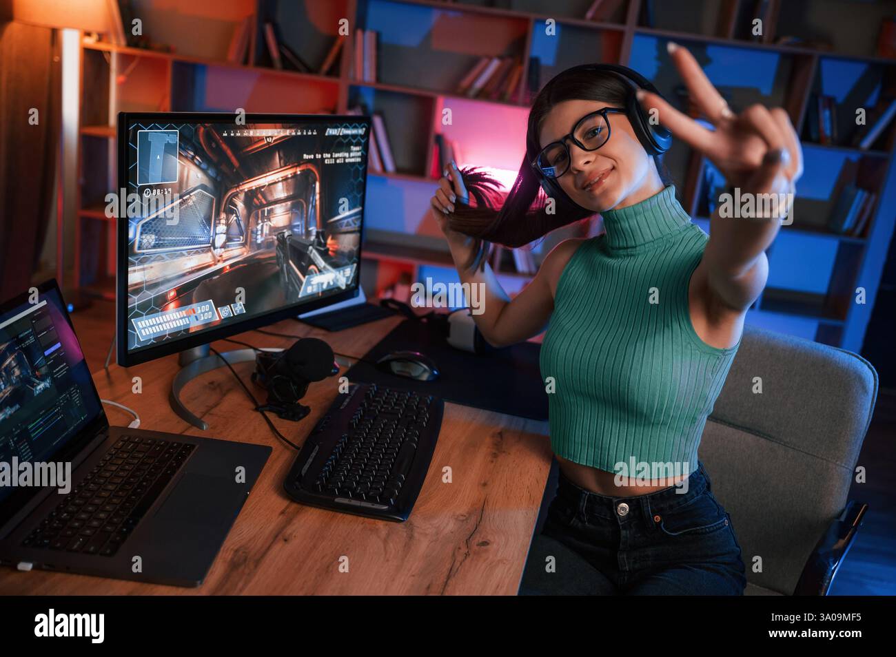 Smiling, showing victory gesture. Young pretty female gamer is playing ...