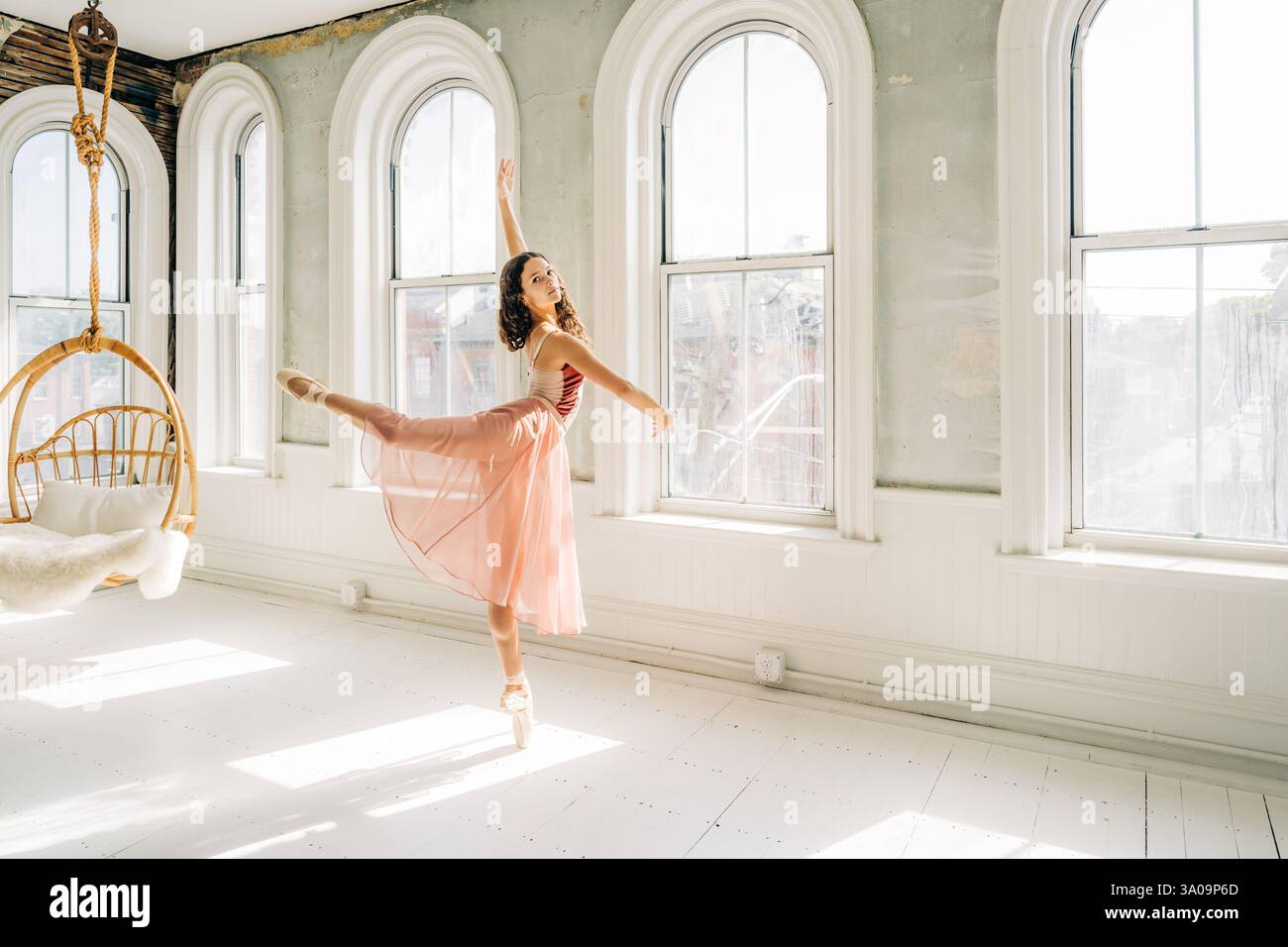 Ballerina performs an arabesque en pointe in a sunlit vintage studio ...
