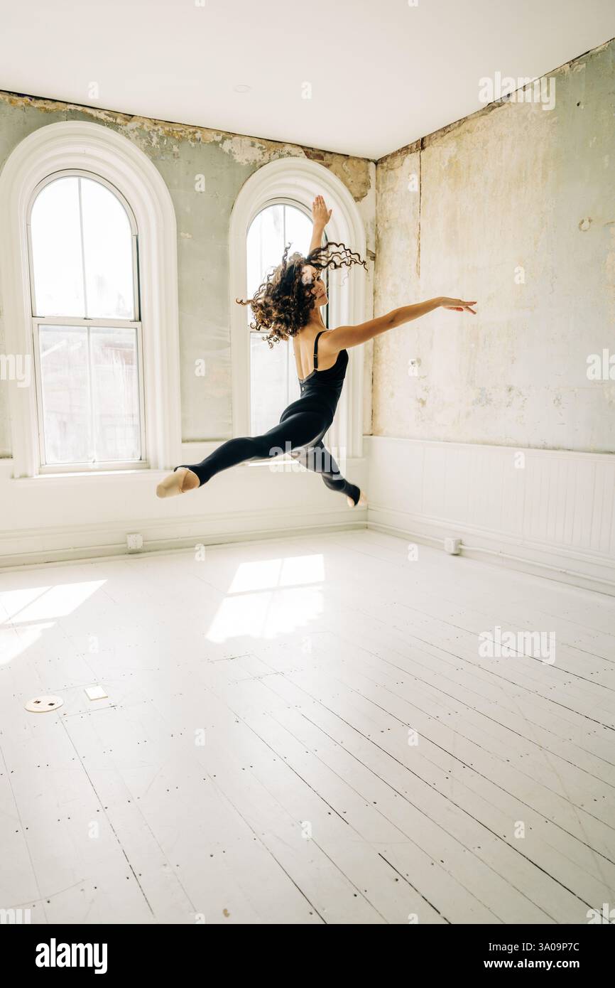 Ballet dancer mid-leap in a black leotard against rustic walls Stock ...