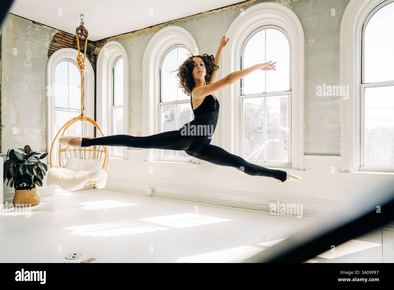 Ballet dancer performs a grand jeté mid-air in a sunlit vintage studio ...