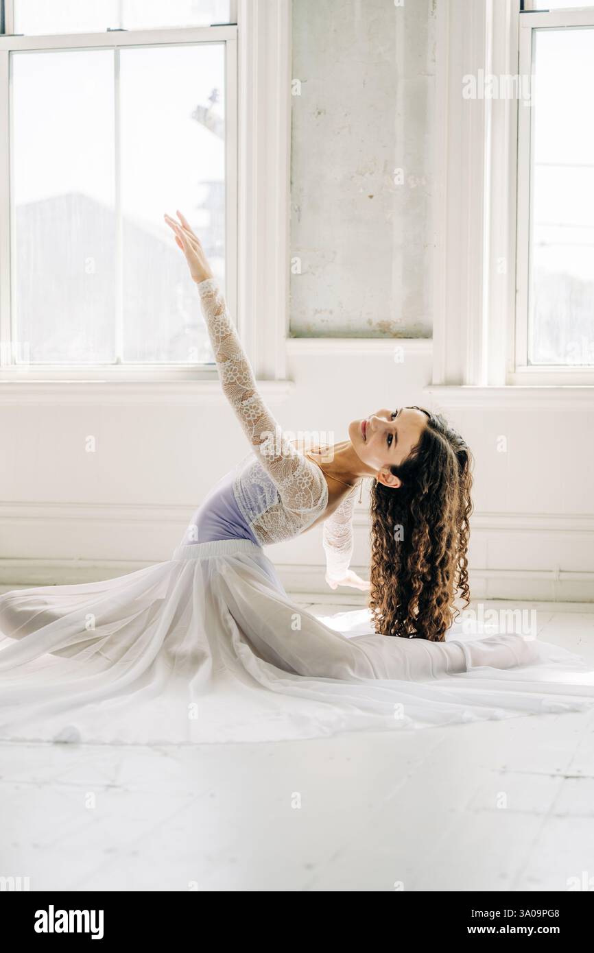 Ballerina gracefully poses on the floor, arching back with elegance ...