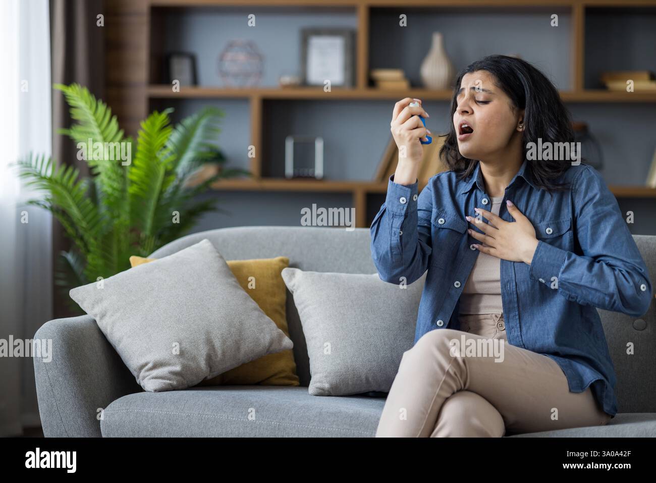 Young woman using an inhaler while sitting on a couch in her living ...