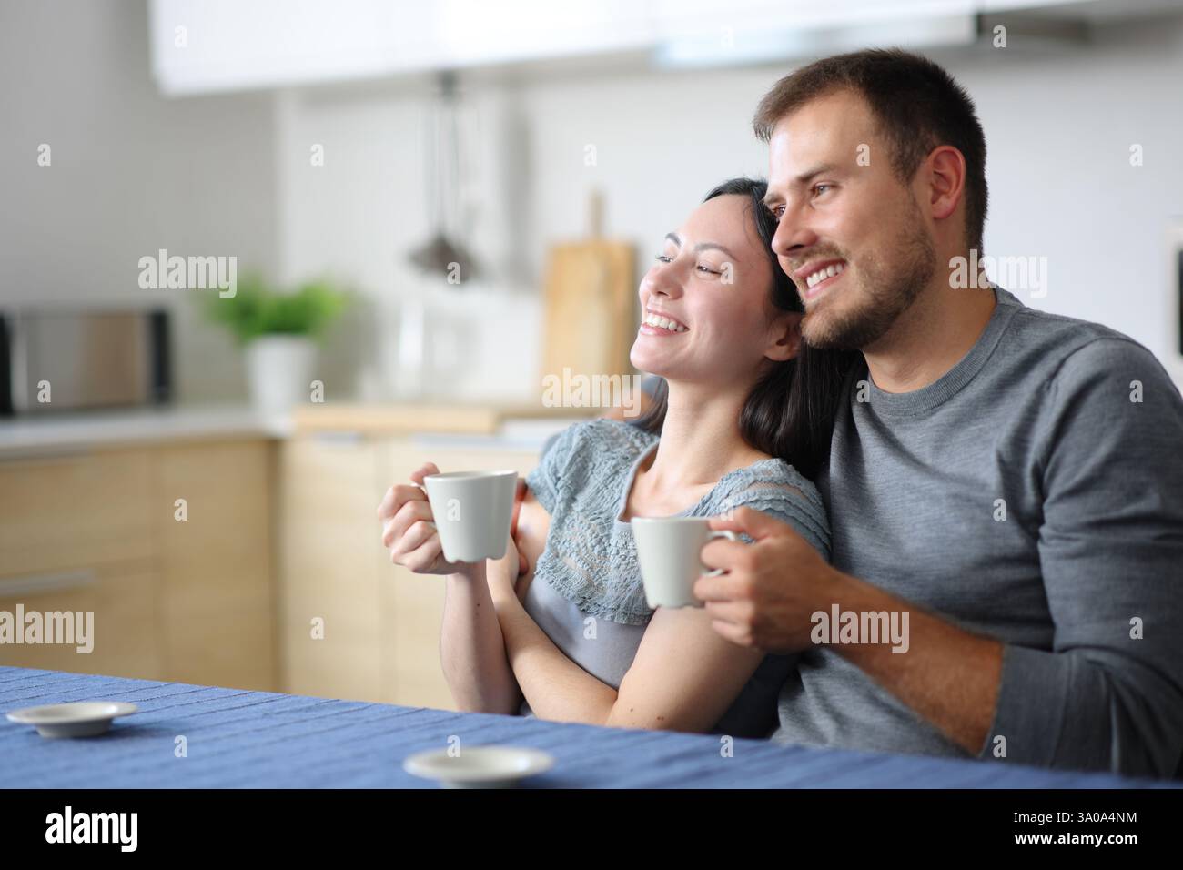 Happy interracial couple drinking coffee contemplating in the kitchen ...