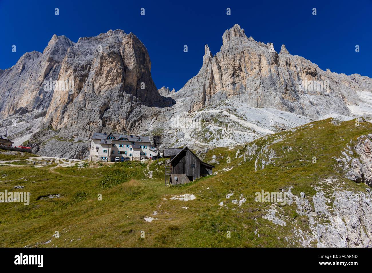A mountain refuge at the base of rugged rock formations under a clear ...