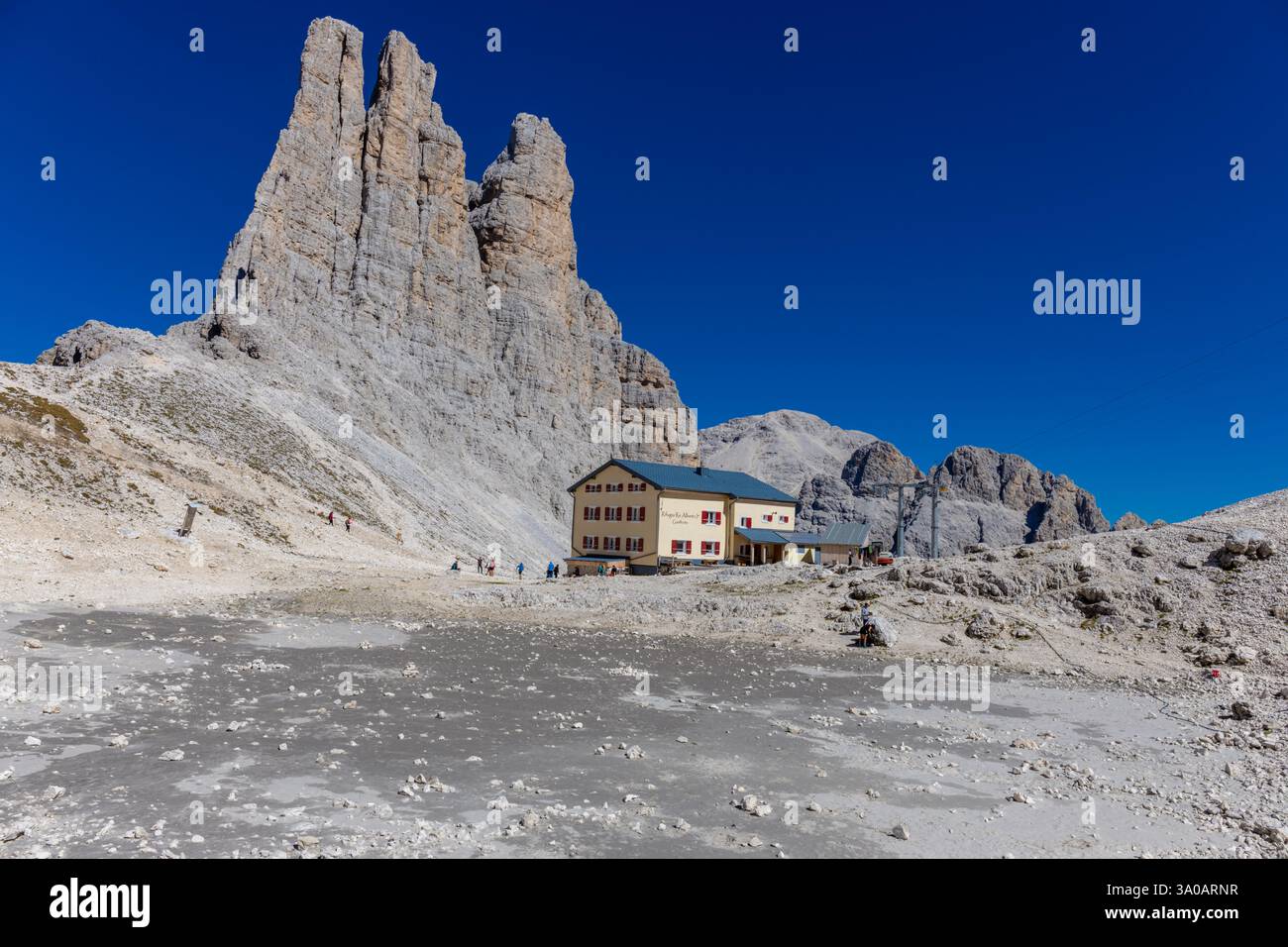 A mountain refuge at the base of rugged rock formations under a clear ...