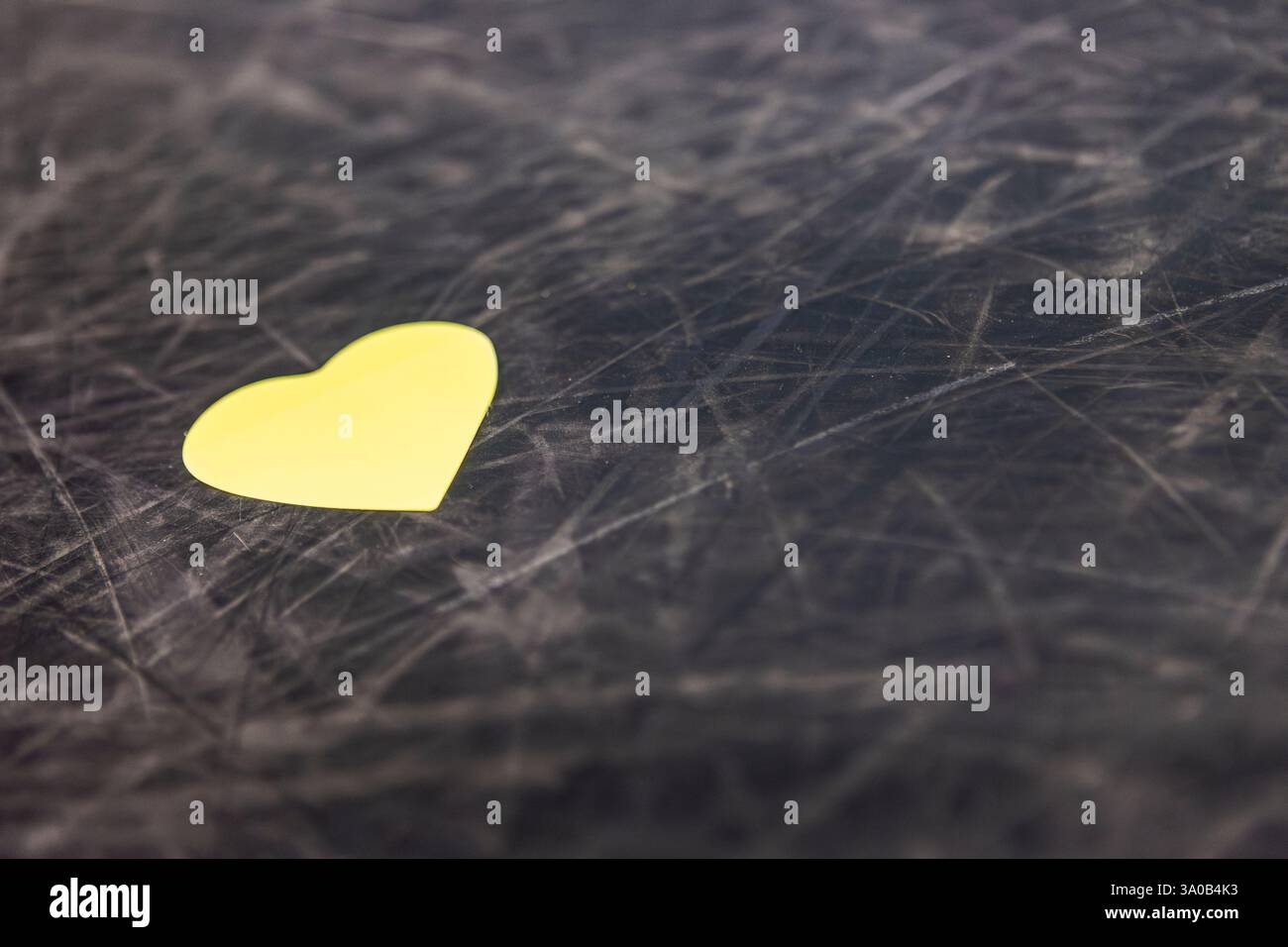 Yellow paper heart shape lying on scratched black surface, representing ...