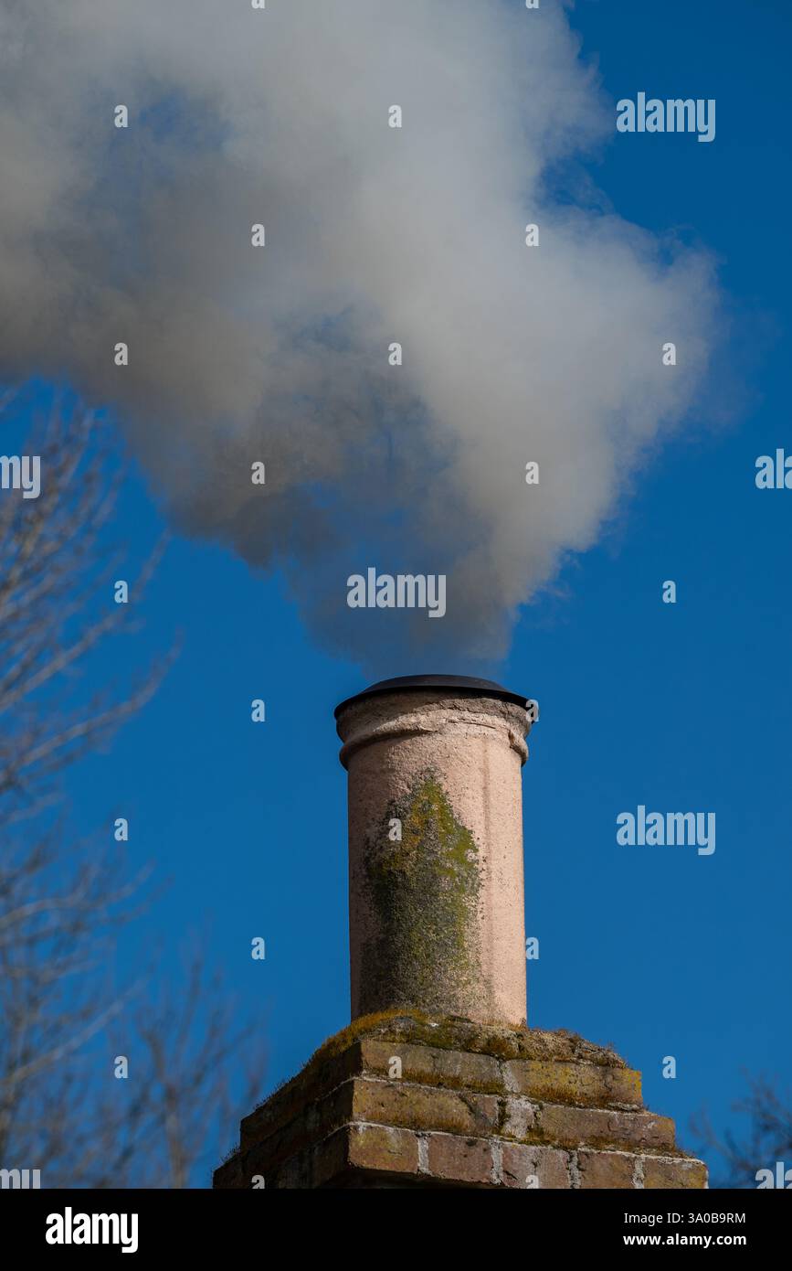 Old chimney puffing out smoke on a sunny day against a blue sky ...