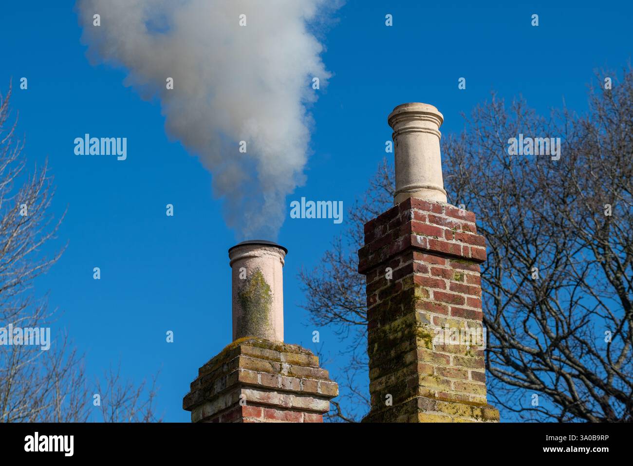 Old chimney puffing out smoke on a sunny day against a blue sky ...