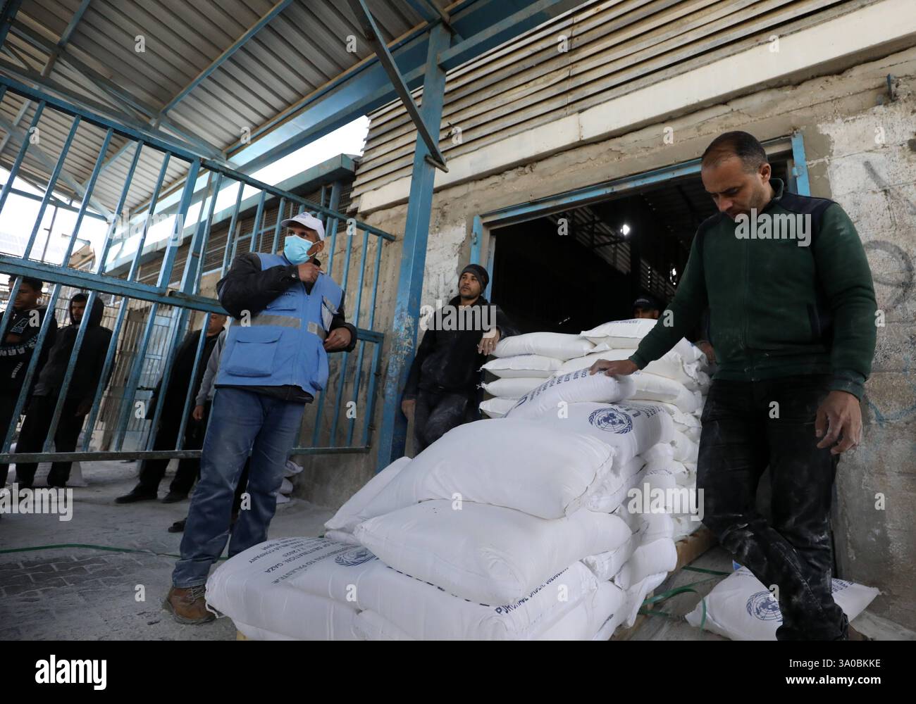 Workers move sacs of flour as Palestinians queue to receive food aid ...