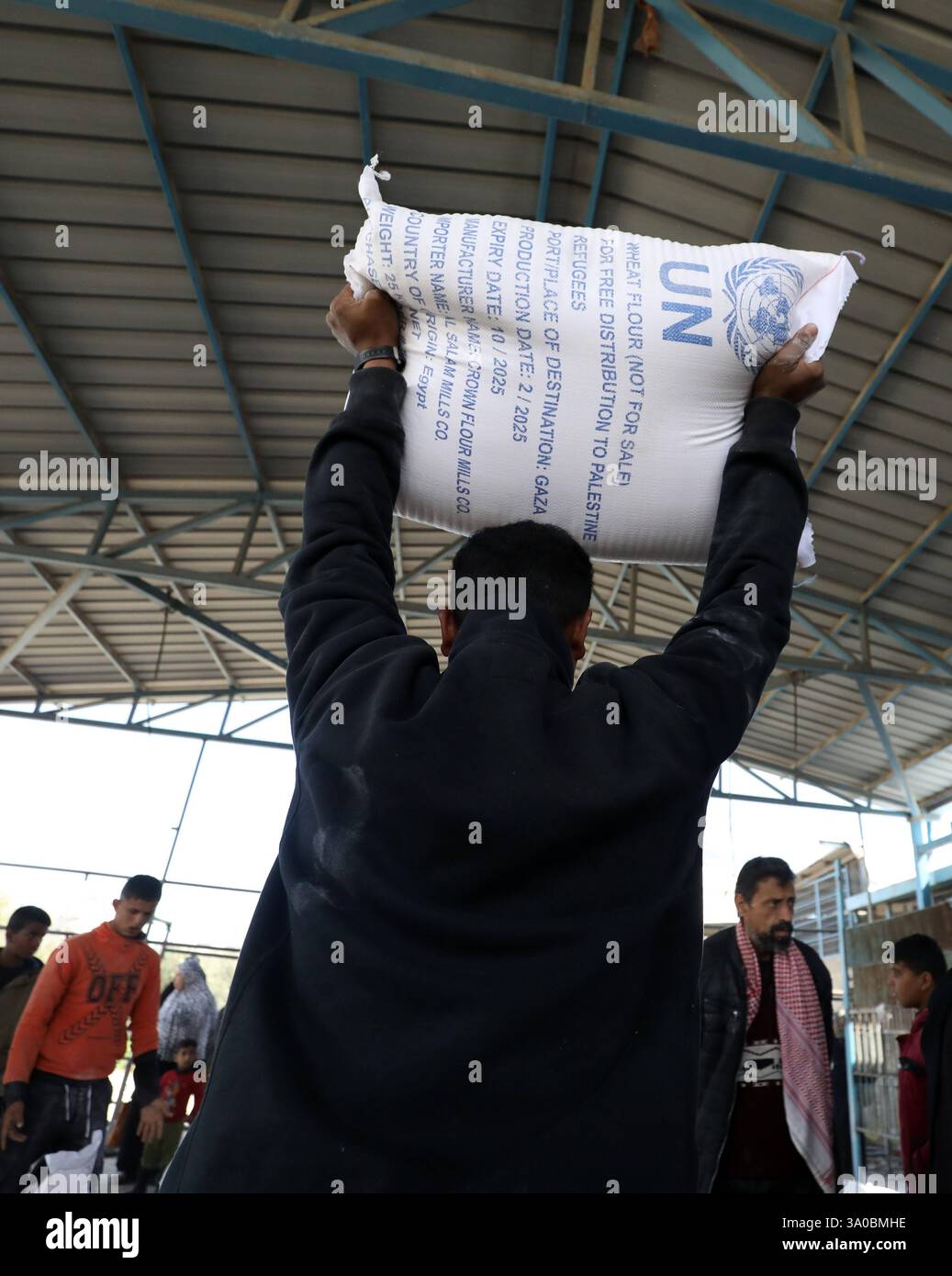 Workers move sacs of flour as Palestinians queue to receive food aid ...