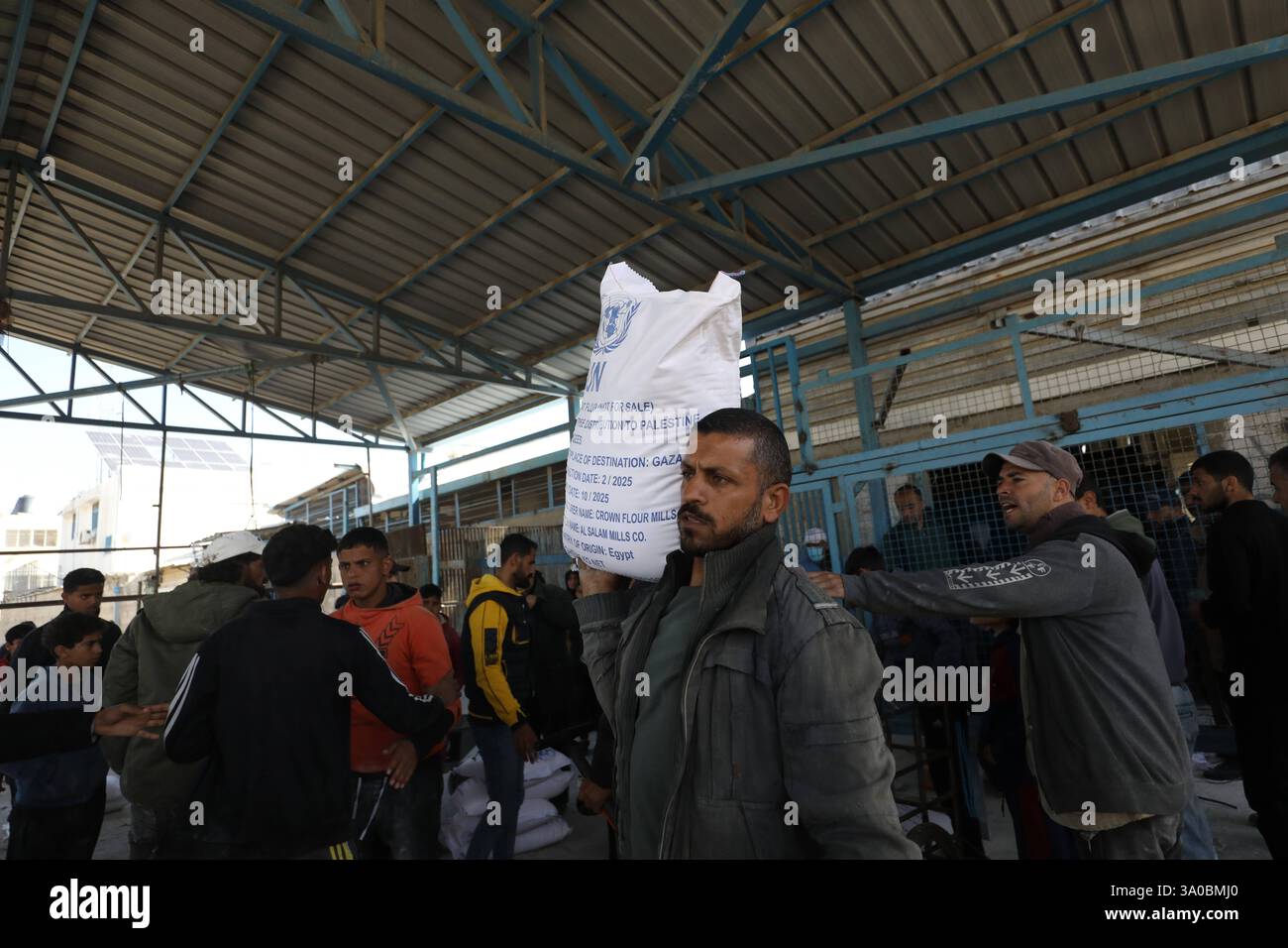 Workers move sacs of flour as Palestinians queue to receive food aid ...