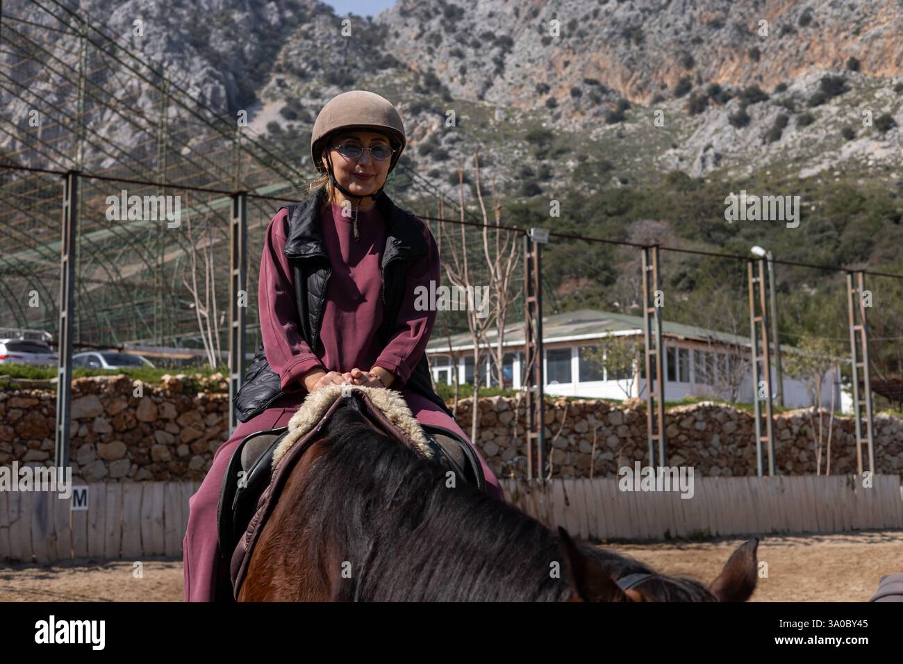 A woman clad in a long outfit and helmet enjoys horseback riding at a ...
