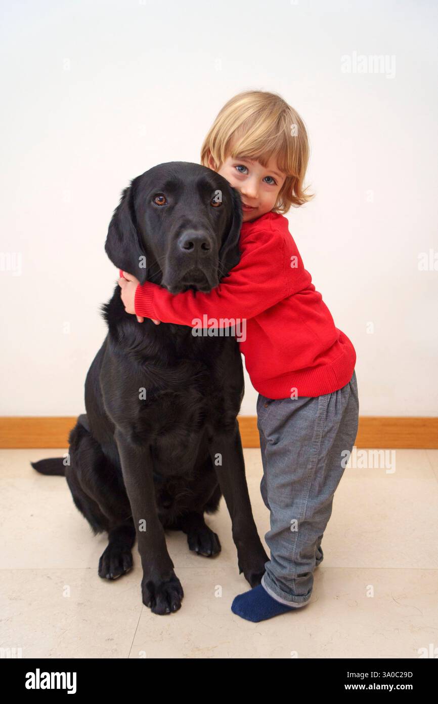 Happy toddler hugging his black labrador retriever dog Stock Photo - Alamy