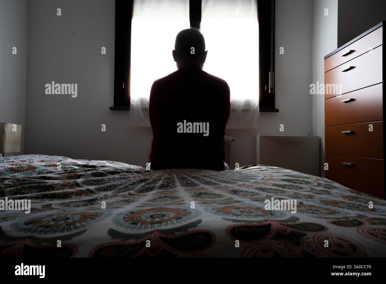 man alone sitting on bed in front of window Stock Photo - Alamy