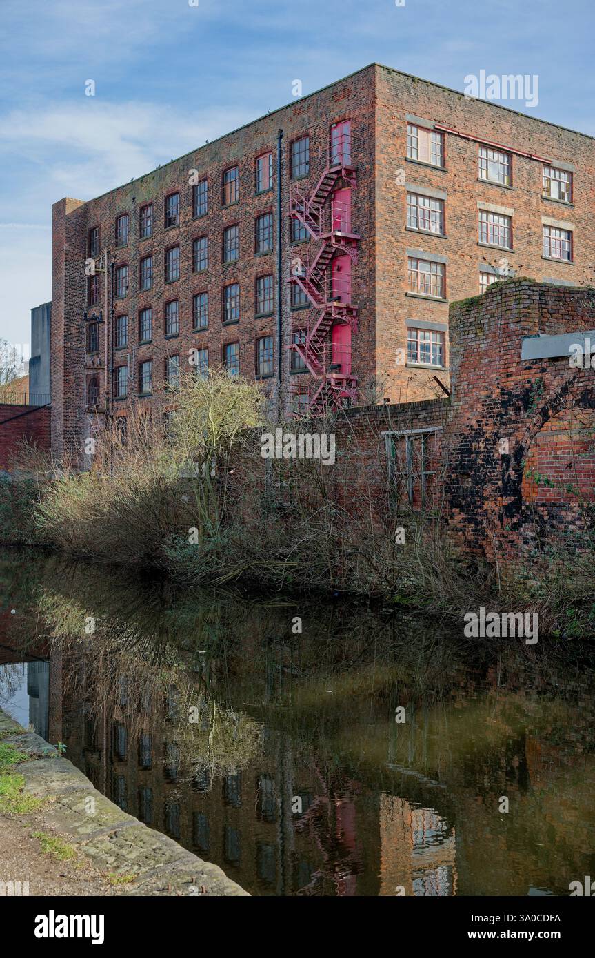 Historic brick factory mill building with red fire escape beside a calm ...