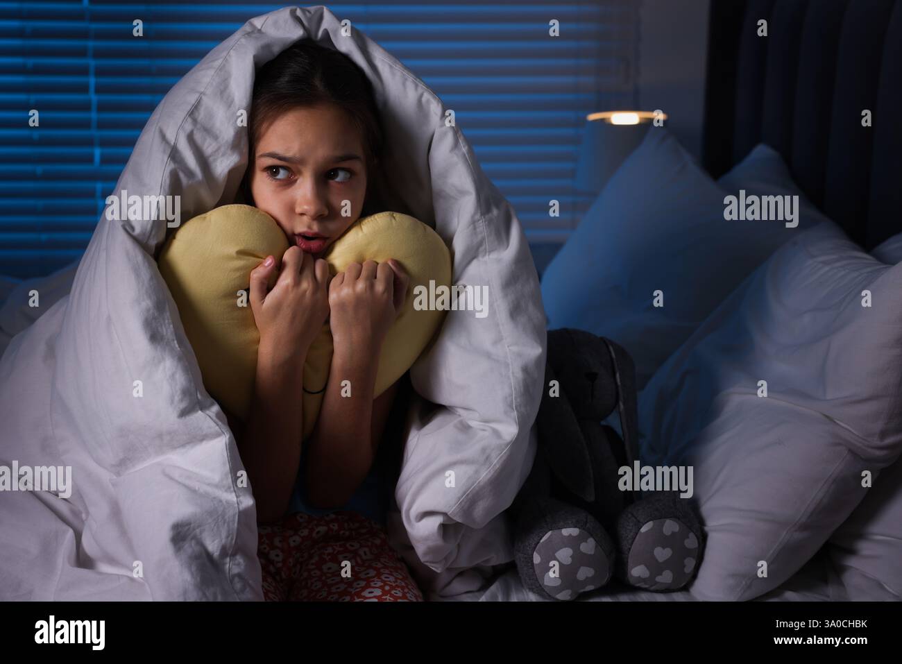 Afraid girl with pillow under duvet on bed at night Stock Photo - Alamy