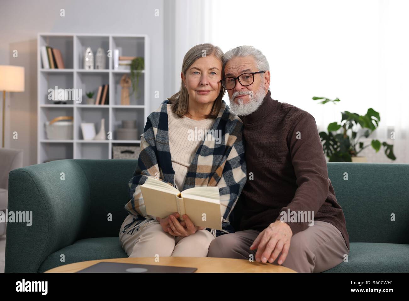 Cute elderly couple reading book together on sofa at home Stock Photo ...