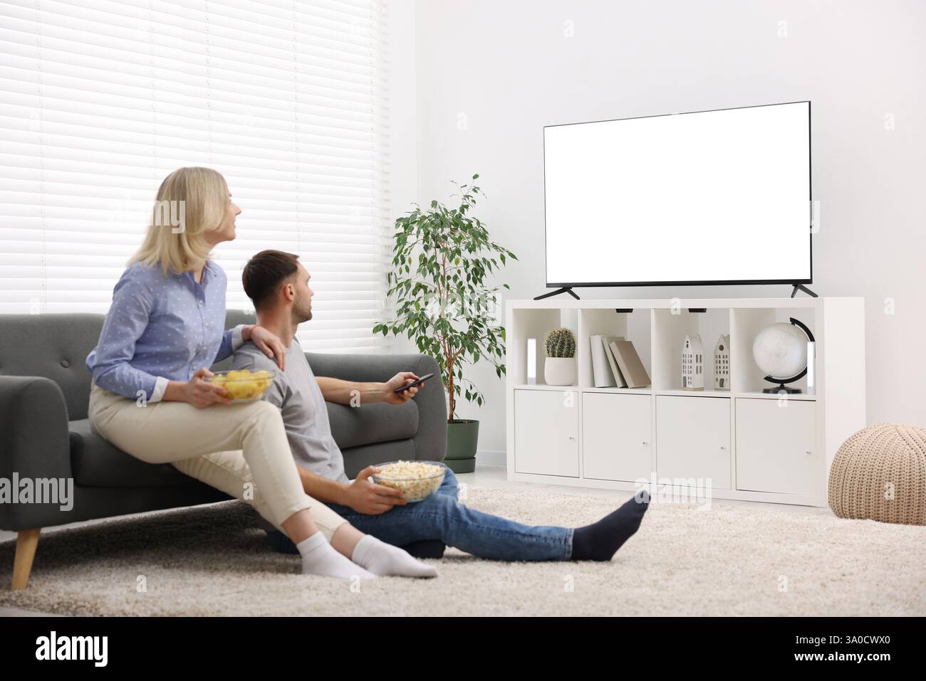 Lovely couple with snacks watching tv at home Stock Photo - Alamy