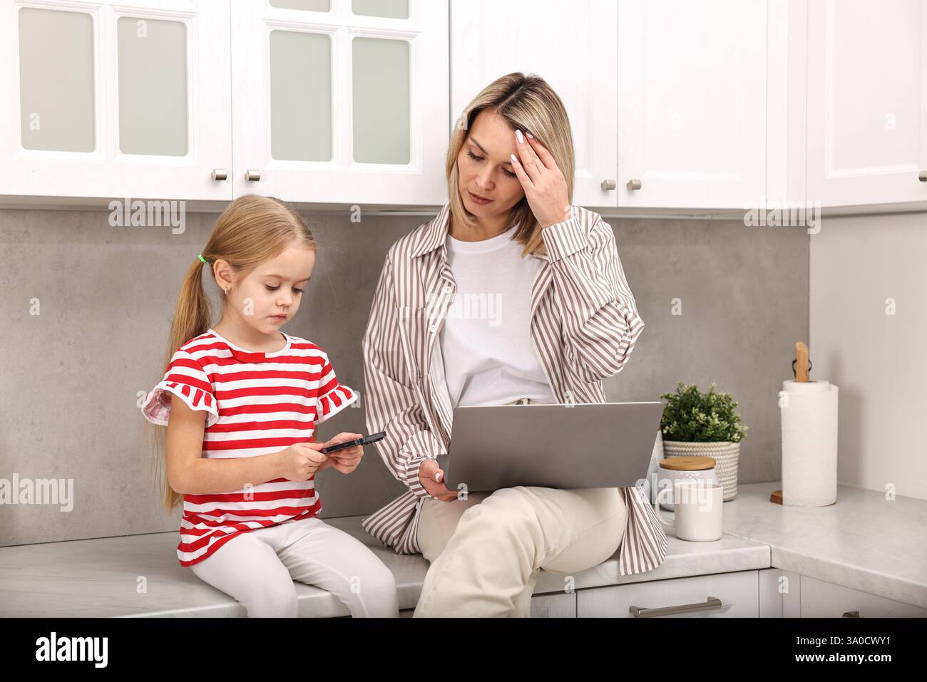 Single mother working with laptop and her daughter in kitchen Stock ...