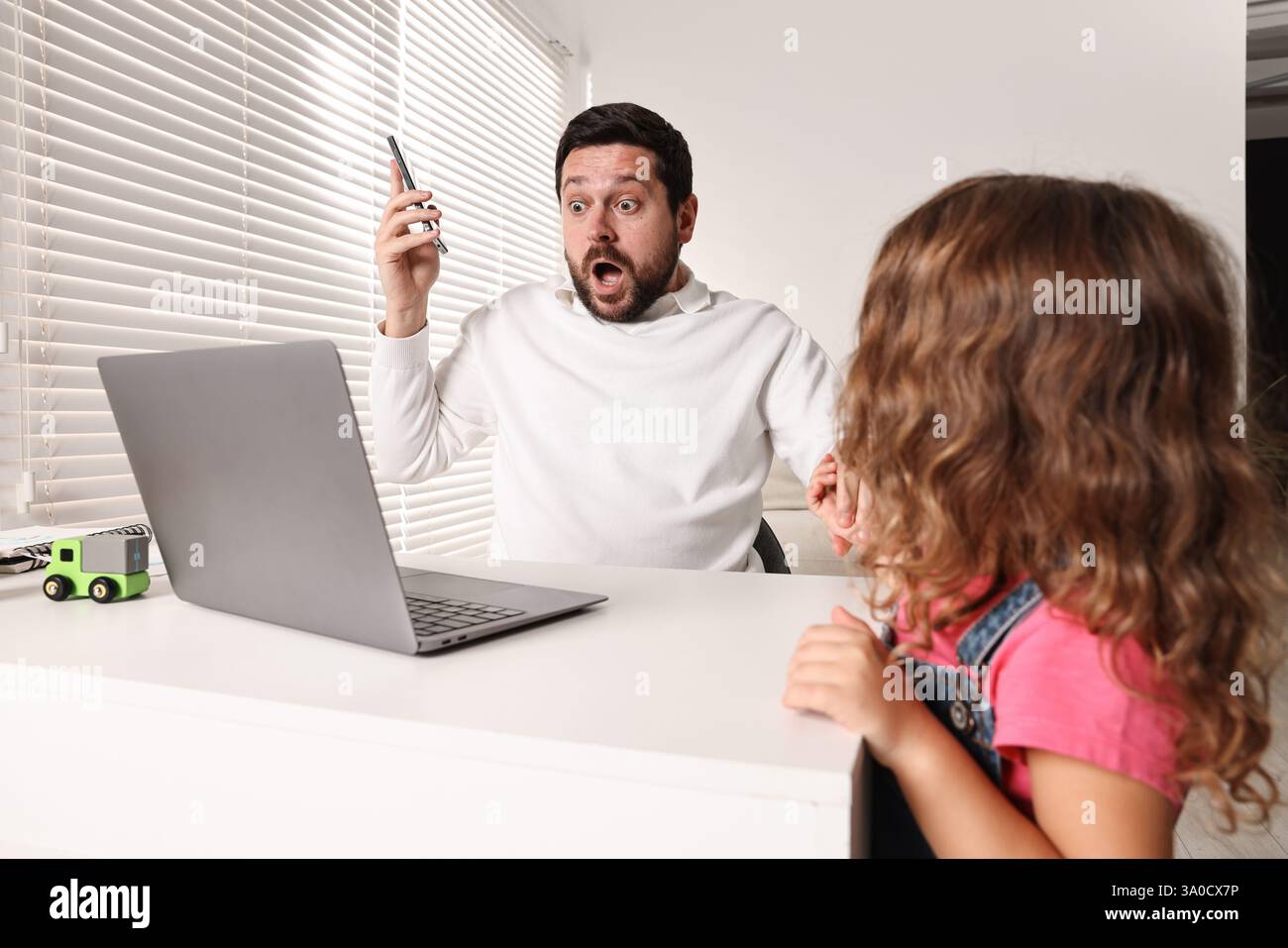 Naughty daughter disturbing her overwhelmed father at table with laptop ...