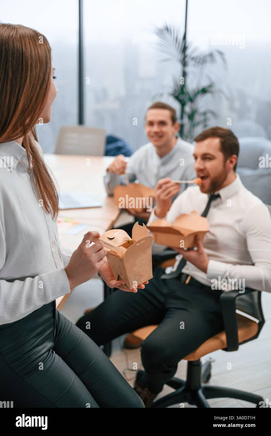 Woman is leaning on the table. Group of coworkers are eating food from ...