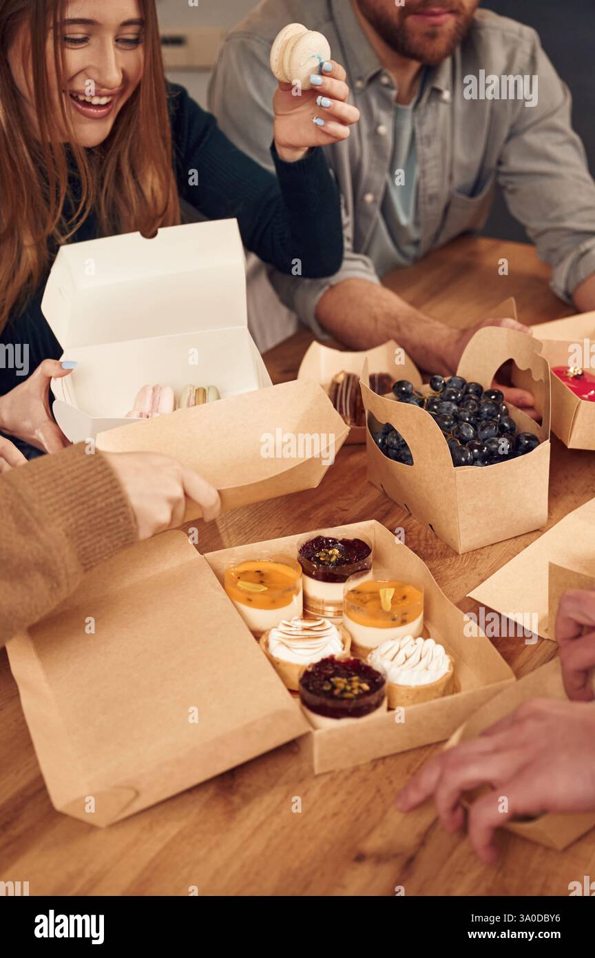 Friends are sitting indoors at home eating macarons, desserts and ...