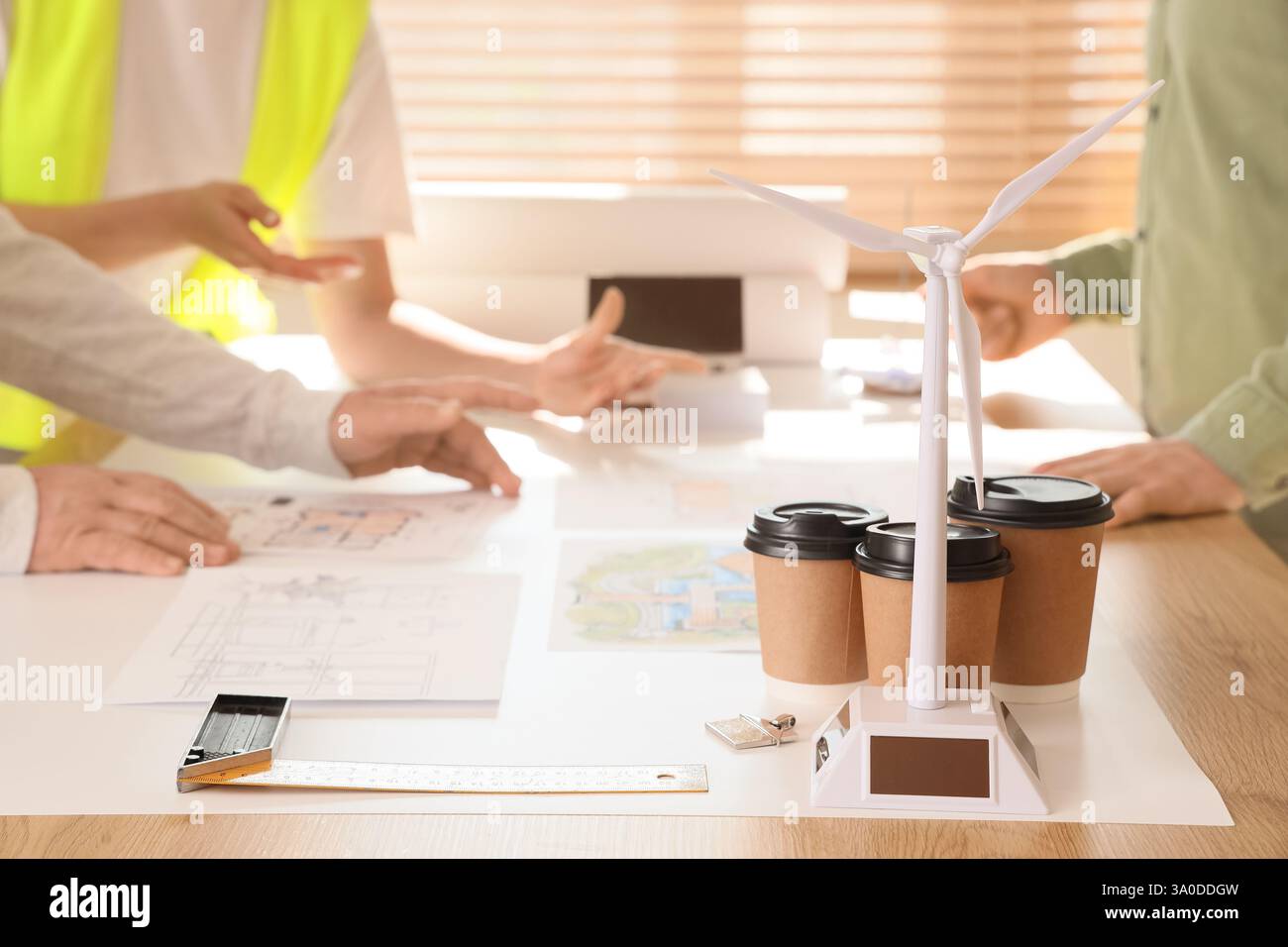 Wind turbine model with cups of coffee on table against engineers ...