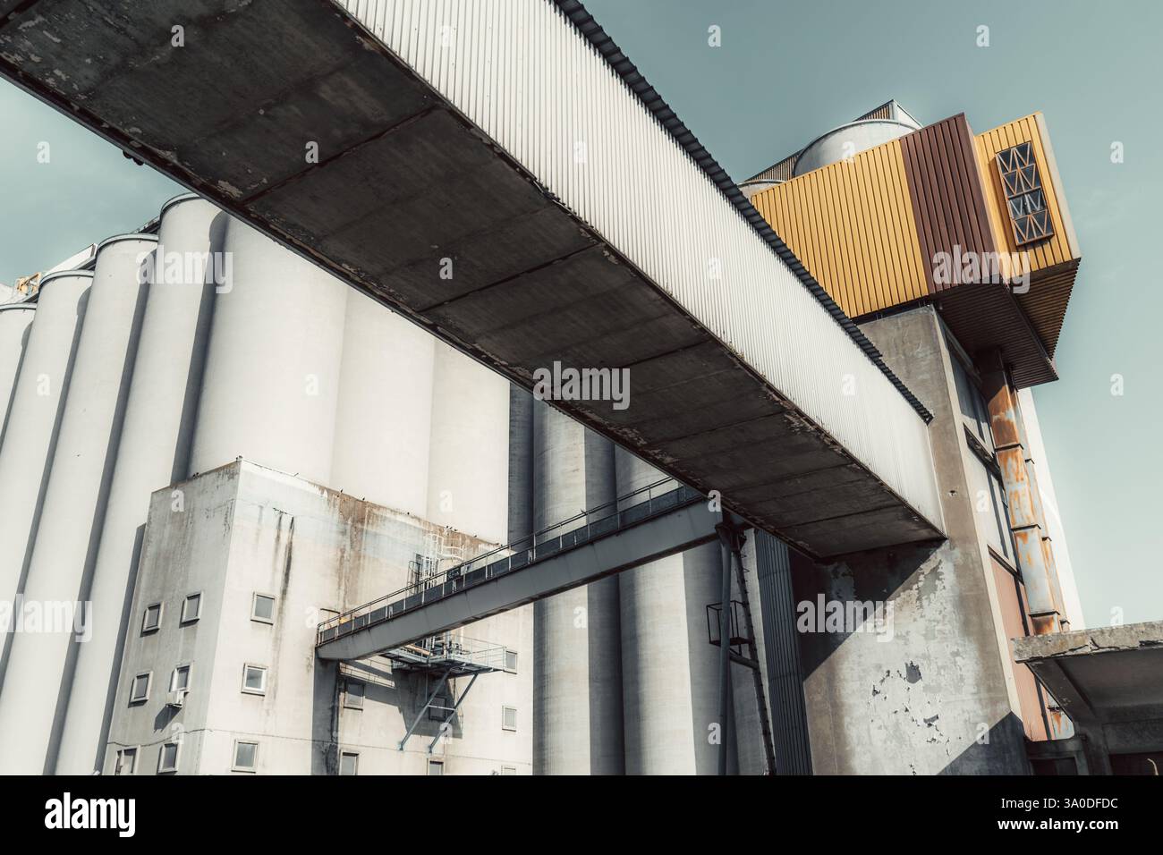 Wide-angle shot of a modern industrial facility with large cylindrical grain silos, a weathered ...