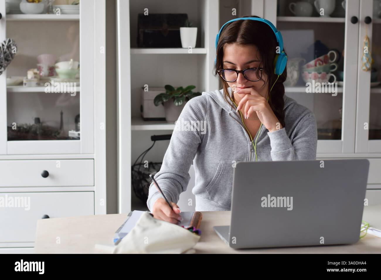 Young girl student writing notes while studying at home using laptop ...