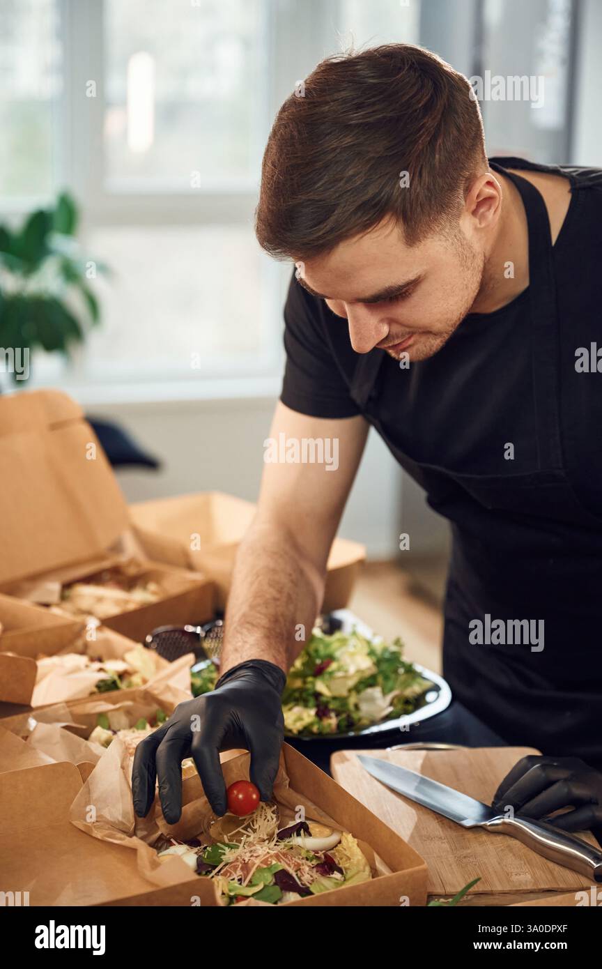 Adding vegetables to the burger. Man is packing food into the paper eco ...