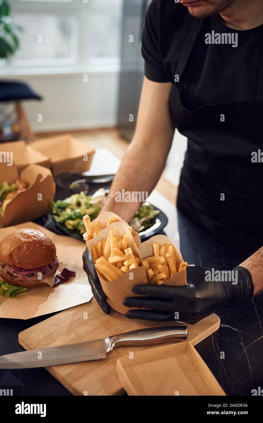 Holding French fries. Man is packing food into the paper eco boxes ...