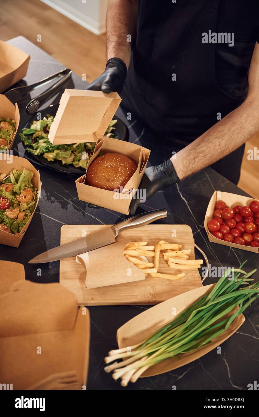 Opening the box with burger. Man is packing food. Indoors, restaurant ...