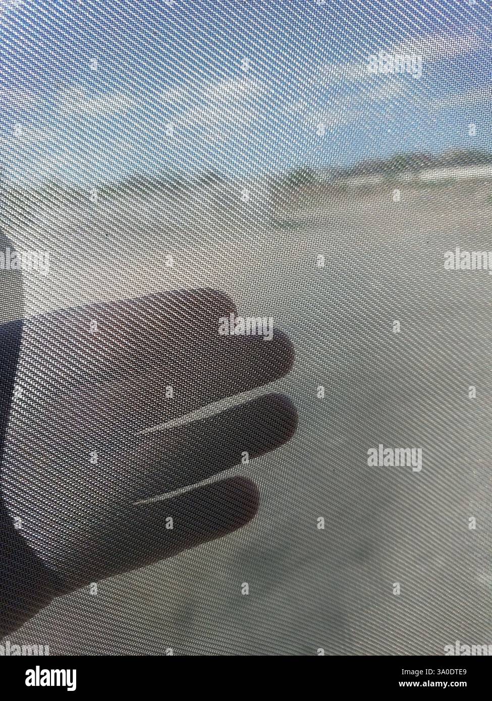 A hand gently presses against a stainless steel mesh screen, blurring ...