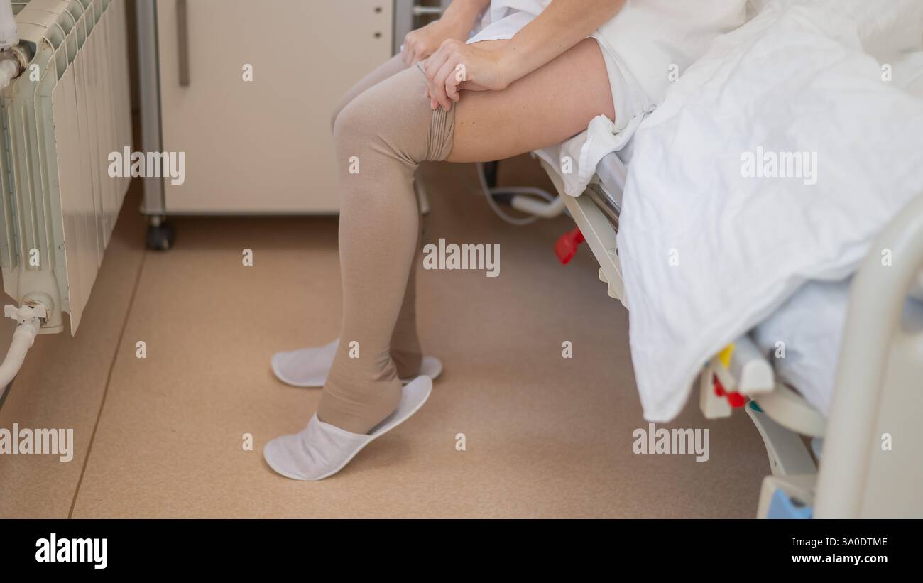 A woman puts on post-operative compression stockings in a hospital room ...