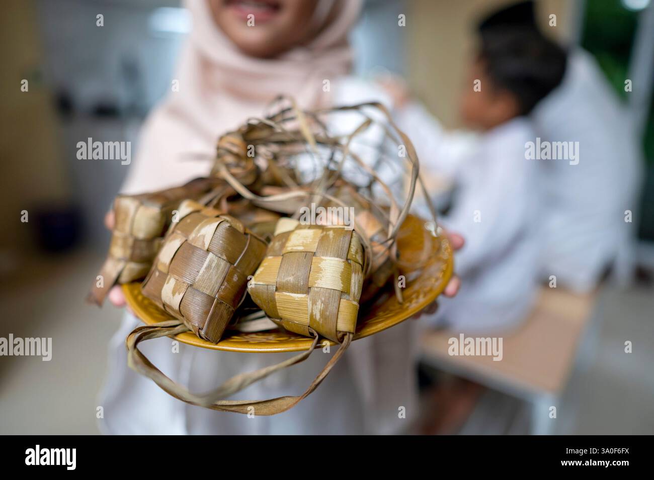 A Muslim girl serving ketupat rice dumpling on the plate for her family ...