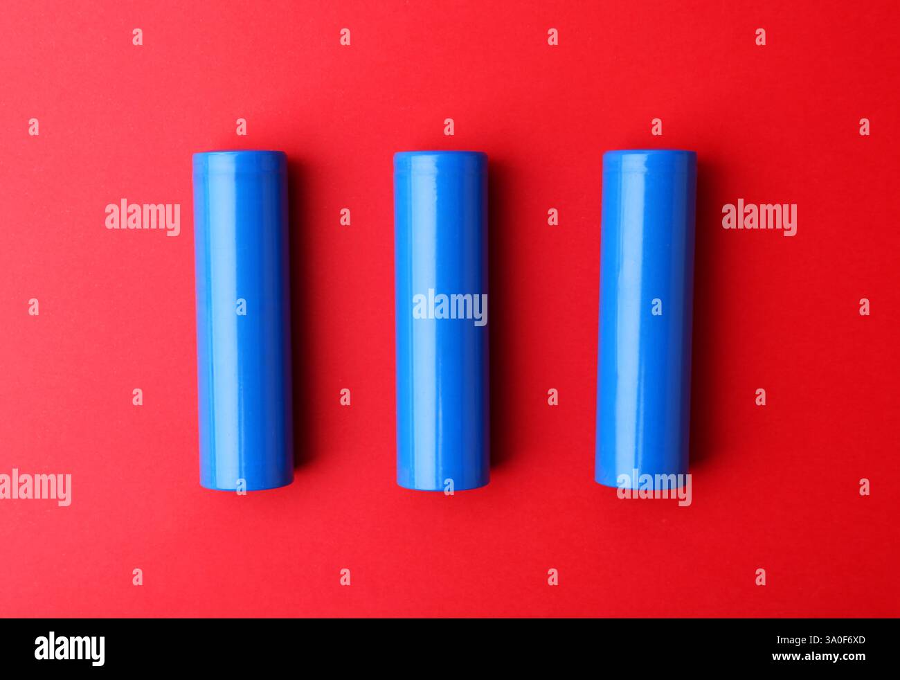 Three AA cell batteries on red background, top view Stock Photo - Alamy
