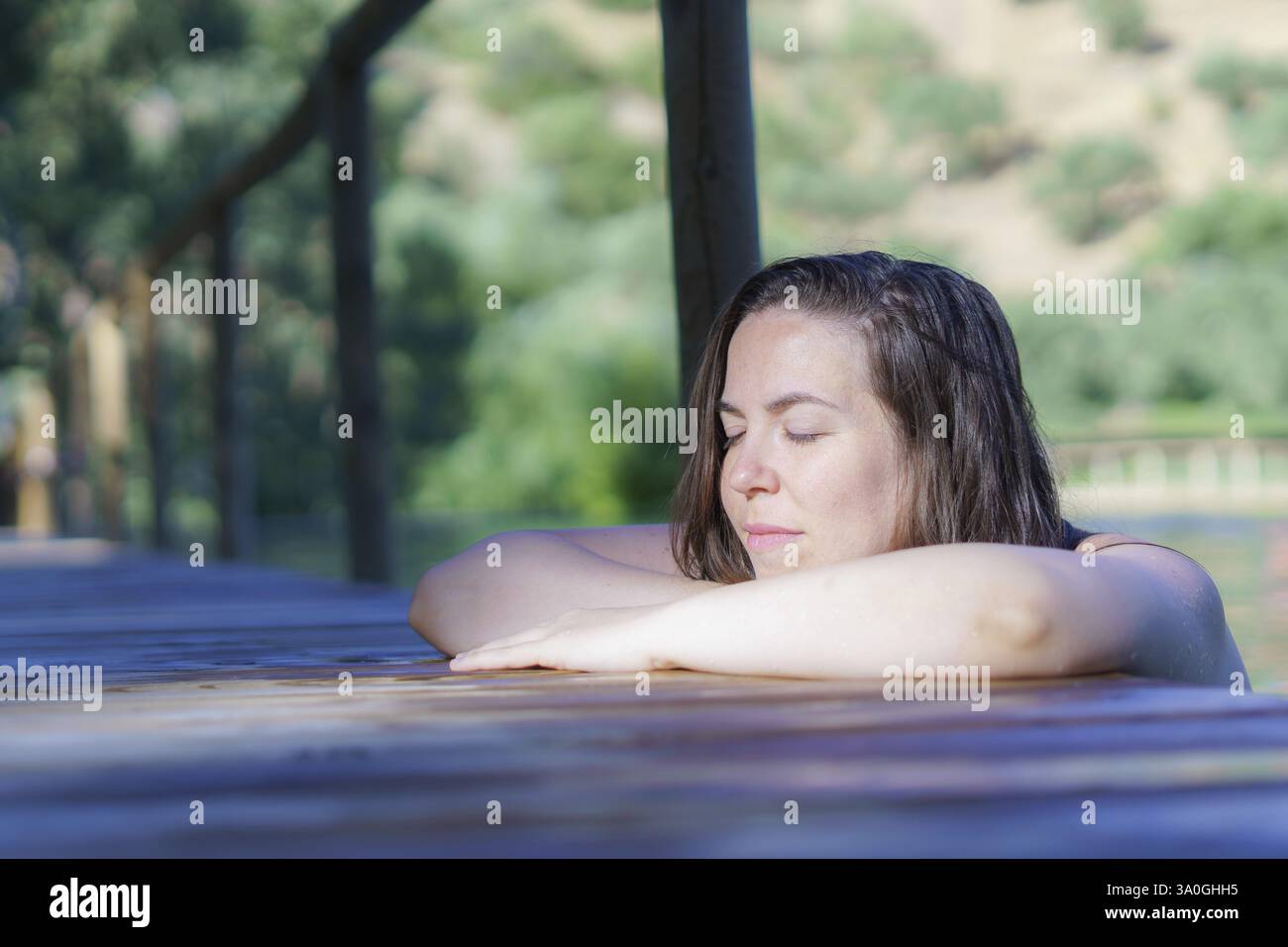 Beautiful brunette woman bathing in a lake lying on a wooden pontoon ...