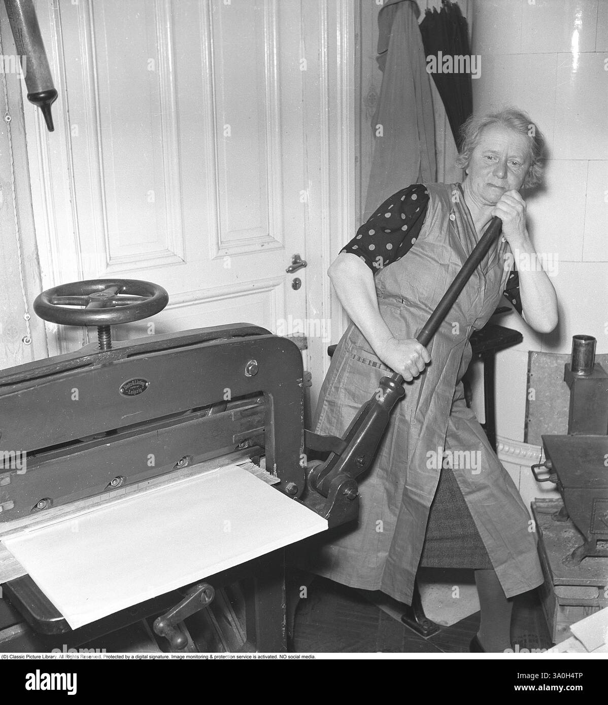 Bookbindery 1947. A lady works at the paper cutting machine. She has ...