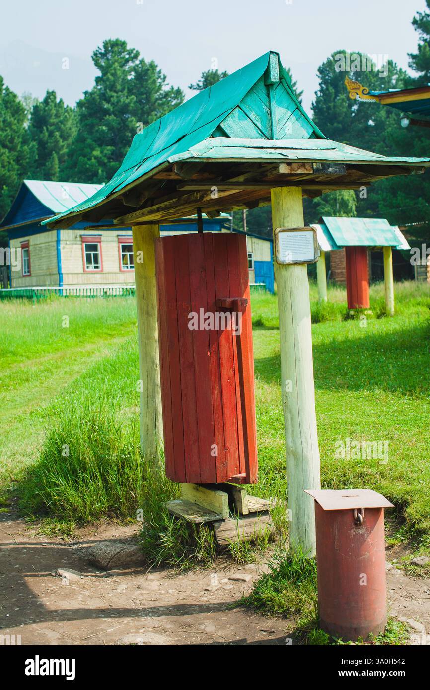 A traditional wooden structure with a red water well under a green roof ...