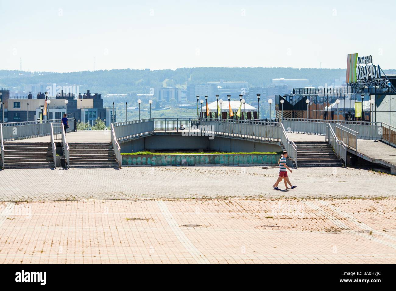 A modern pedestrian walkway with railings and lampposts leads toward a ...