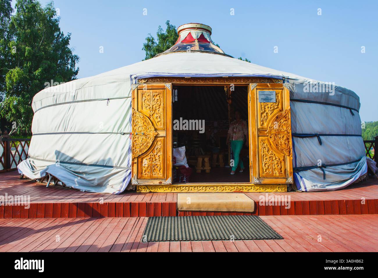 A traditional yurt with intricately carved wooden doors, set on a red ...