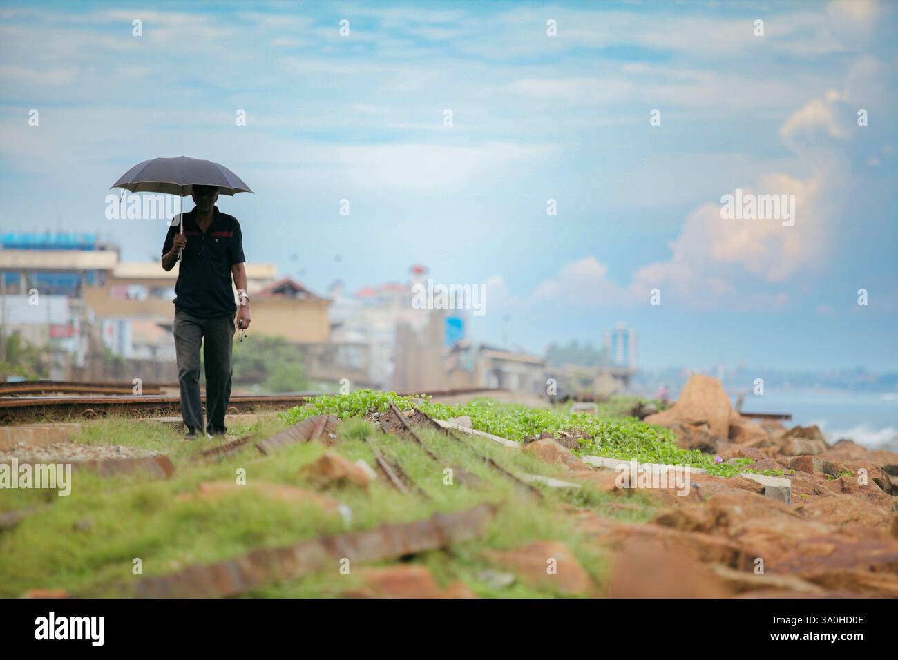 A person carrying an umbrella strolls along overgrown railway tracks ...